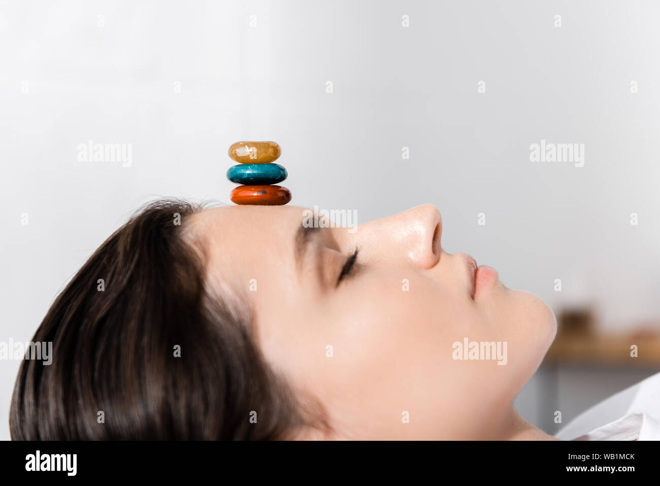 woman lying with closed eyes with colorful stones on forehead Stock ...