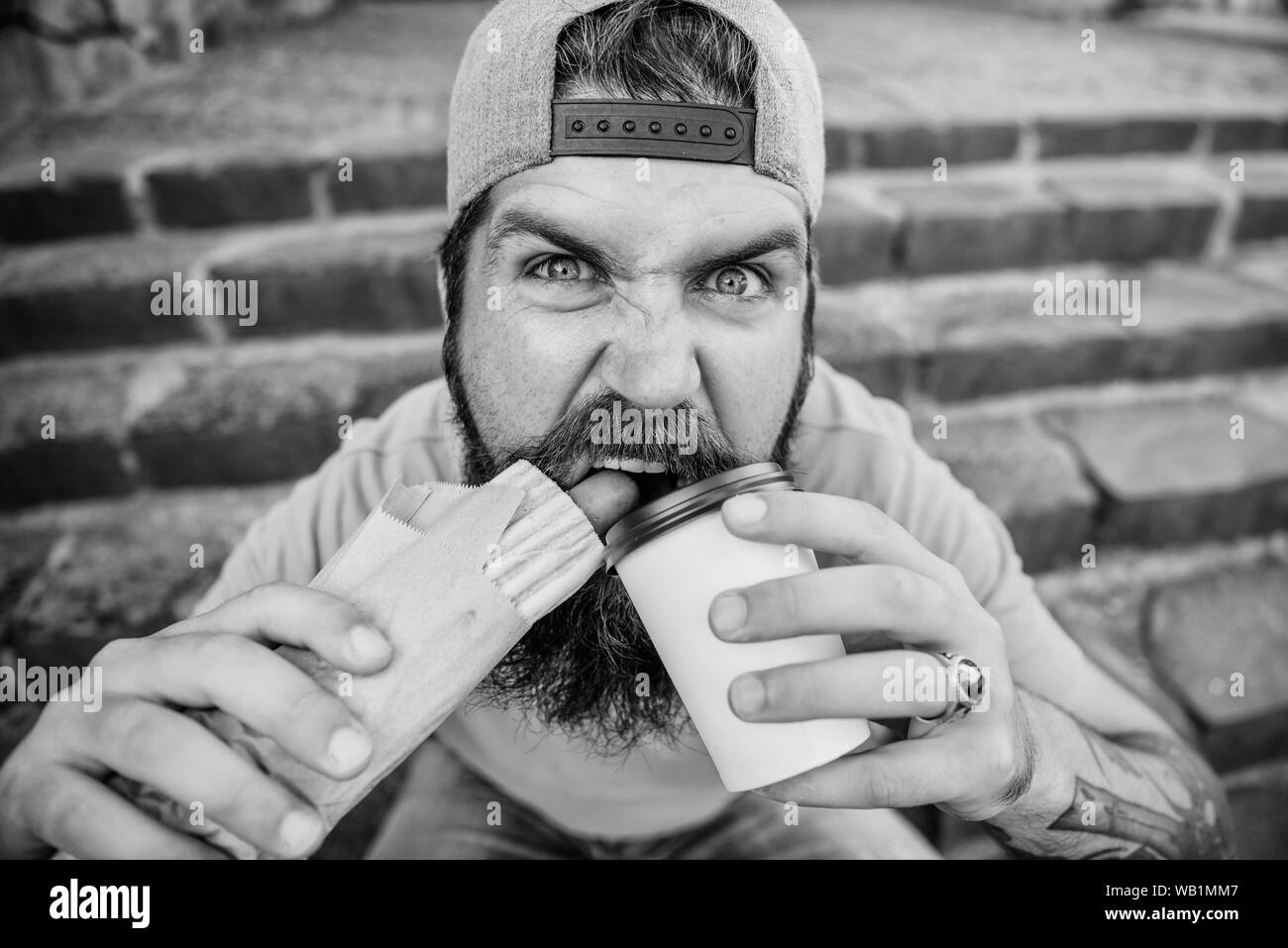 Always fresh and tasty hot dog. Hungry guy biting hot dog and sipping ...