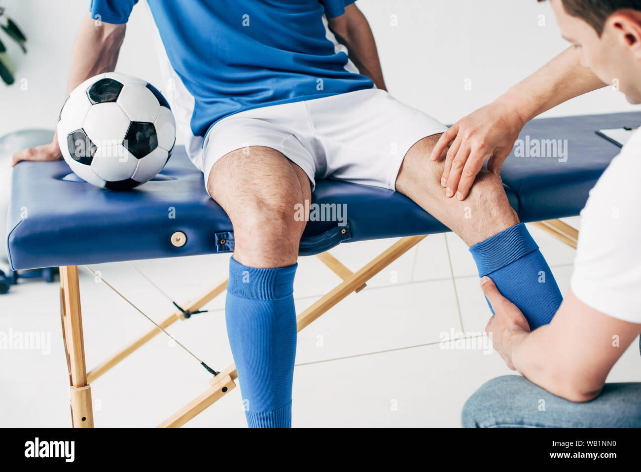 partial view of Physiotherapist massaging leg of football player in ...