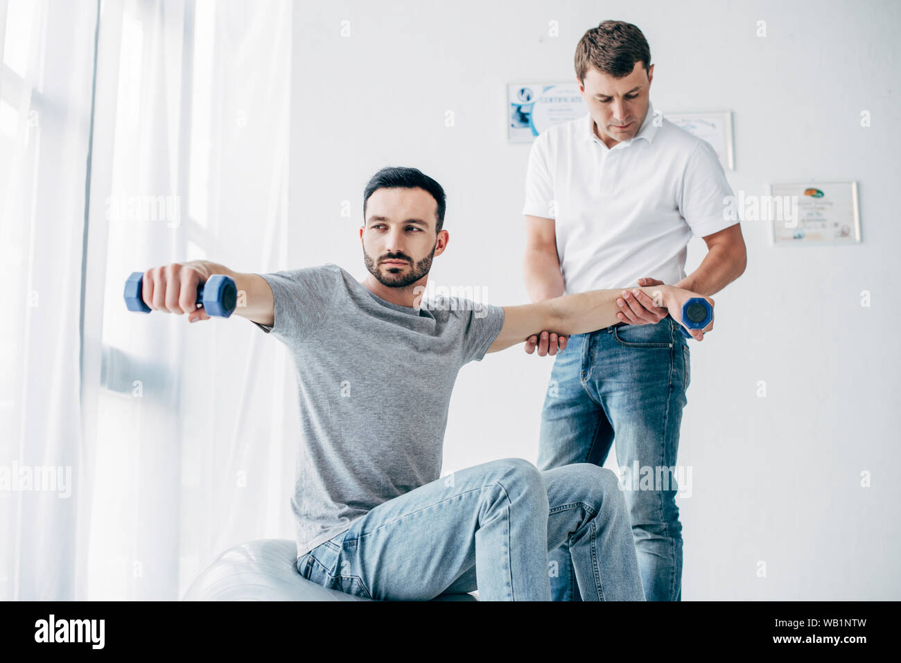 chiropractor stretching arm of good-looking patient with dumbbells in ...