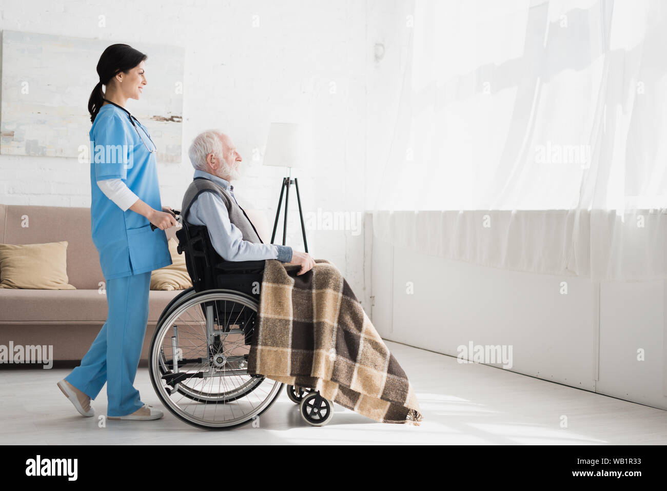 Side view of happy nurse standing in room with copy space, and carrying ...