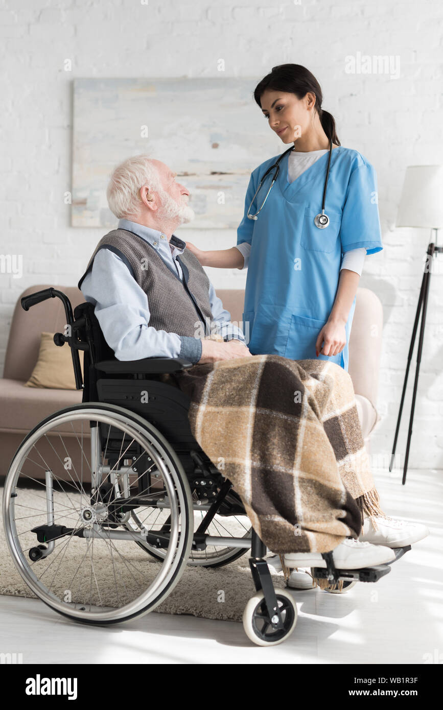 Nurse putting hands on disabled grey haired man in wheelchair Stock ...