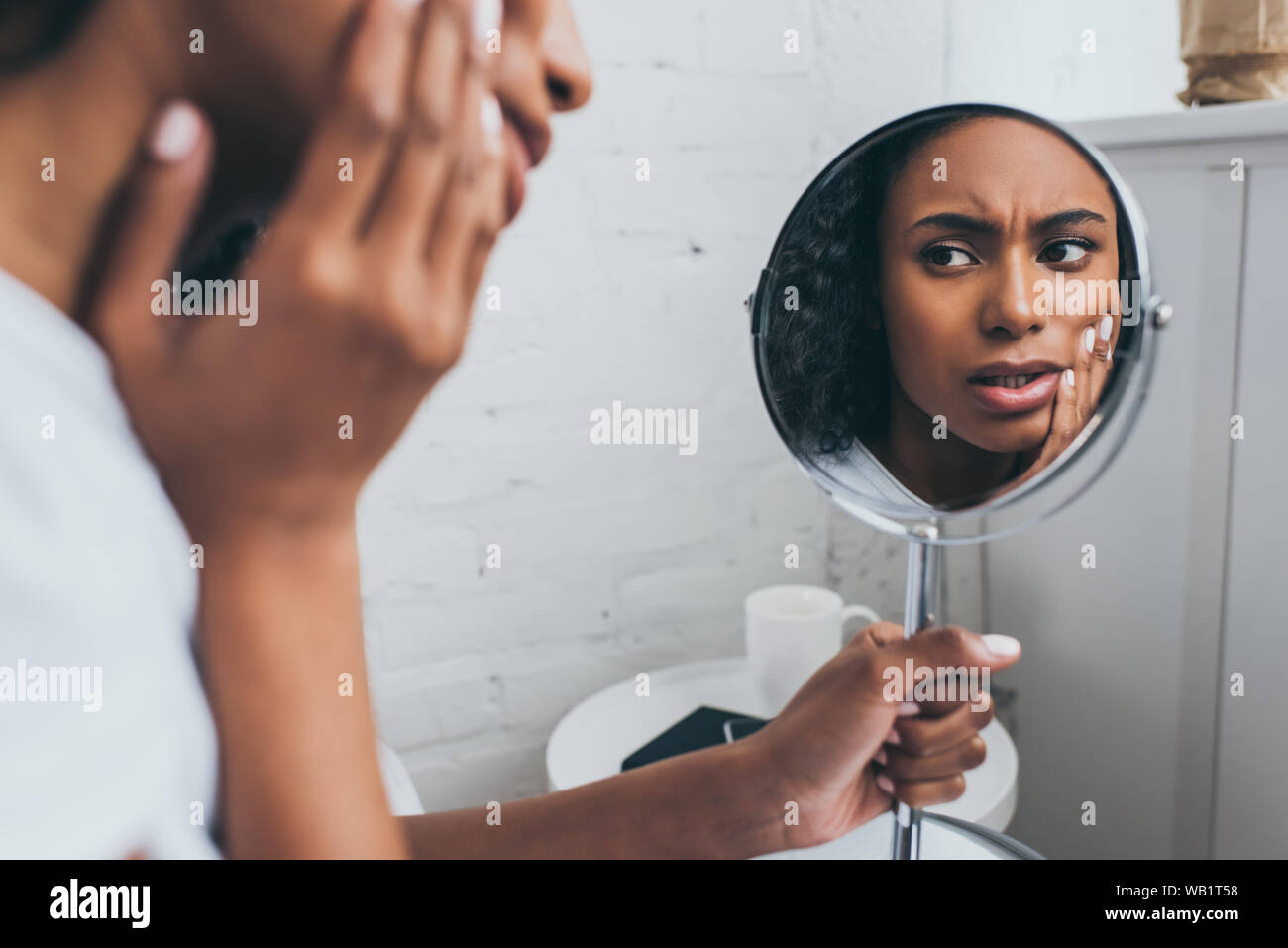 pretty african american woman looking at mirror while suffering from ...