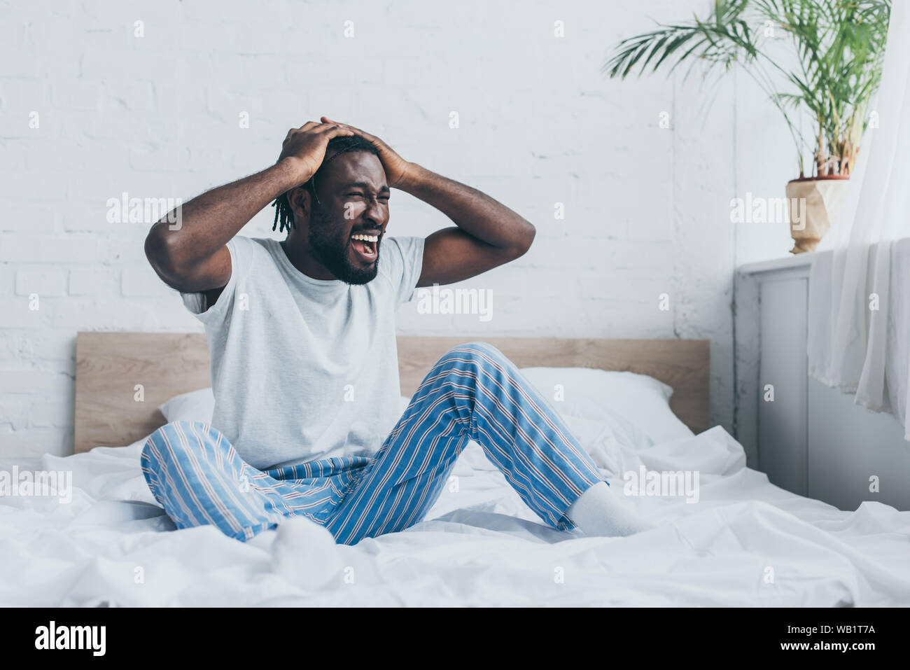african american man screaming while suffering from headache in bedroom ...