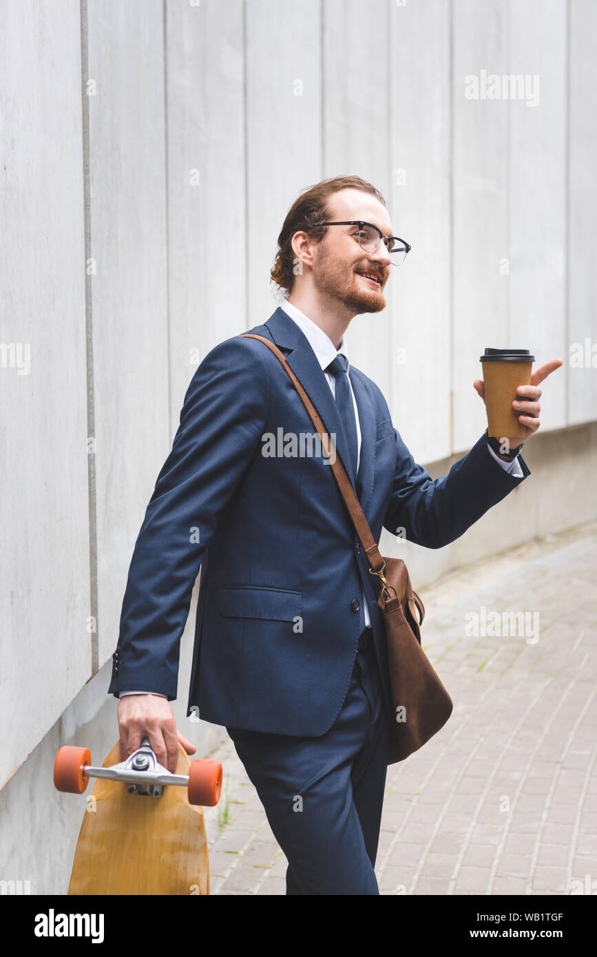 happy businessman in formal wear holding skateboard with paper cup in ...