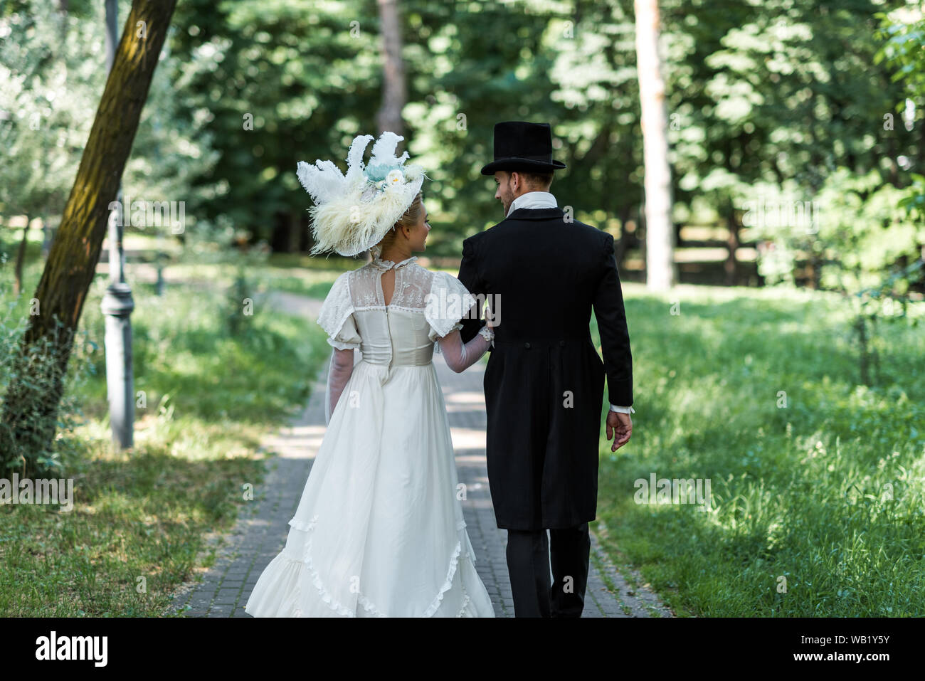 victorian man and woman in hats walking outside near green trees Stock ...