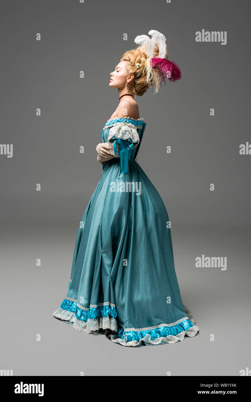 side view of pompous victorian woman in wig standing in blue dress on ...