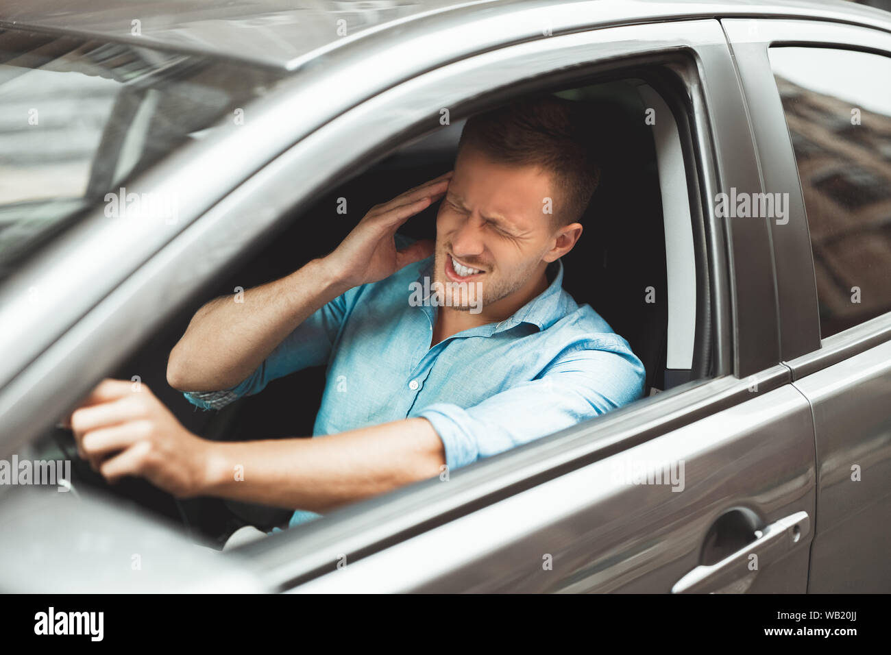 young handsome man suffering from headache while driving in his car ...