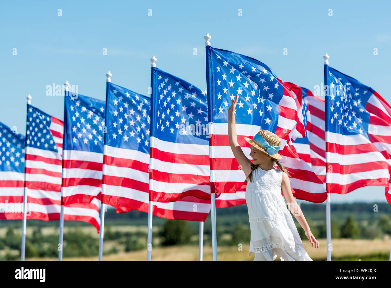 cheerful patriotic child standing in white dress near american flags ...