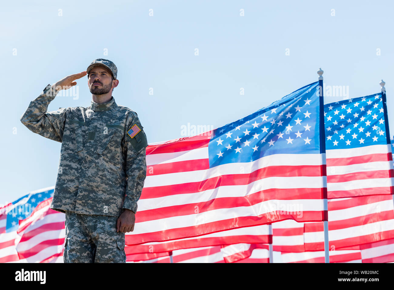 handsome soldier in military uniform giving salute near american flags ...