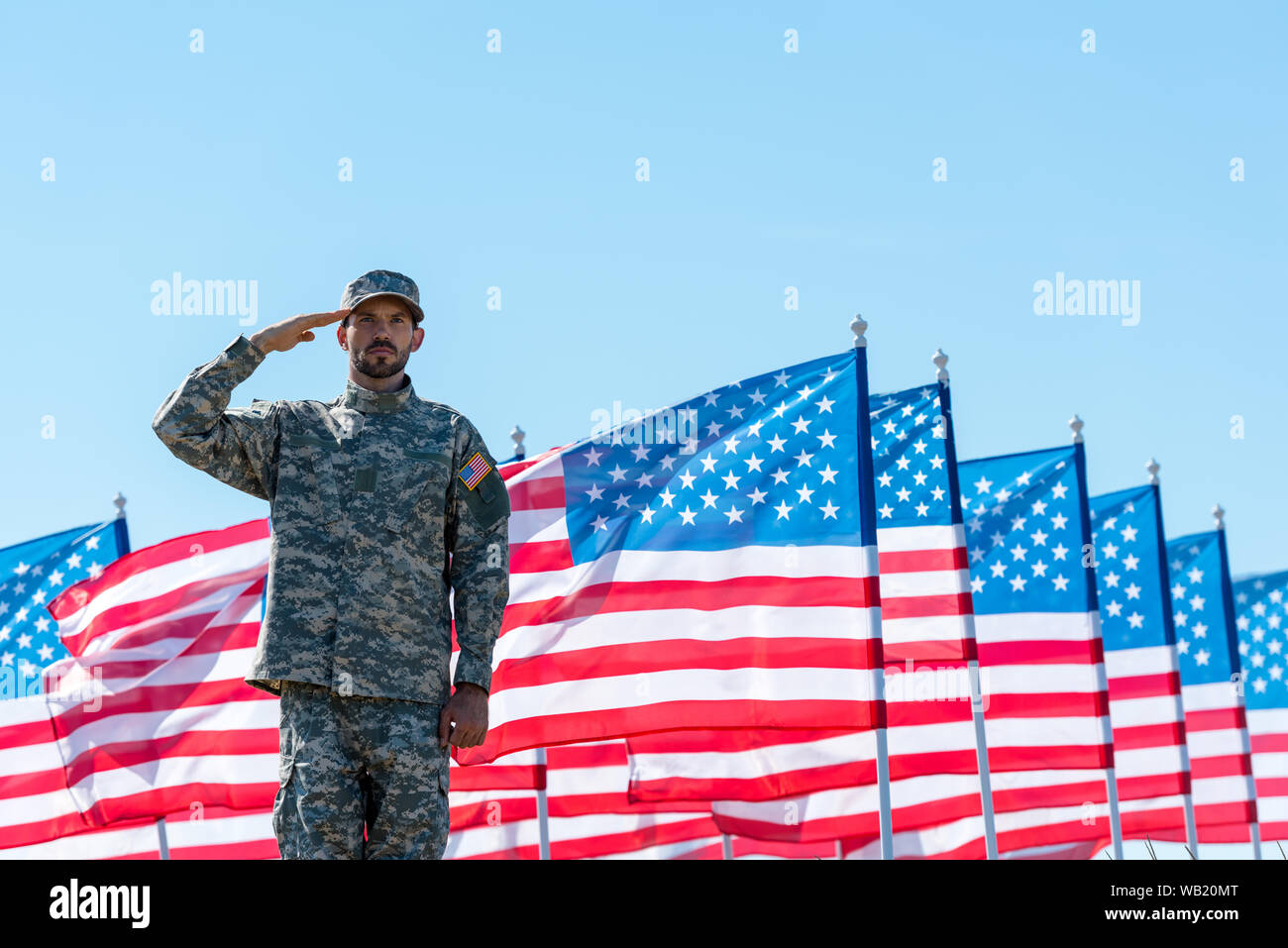 man in military uniform giving salute near american flags with stars ...