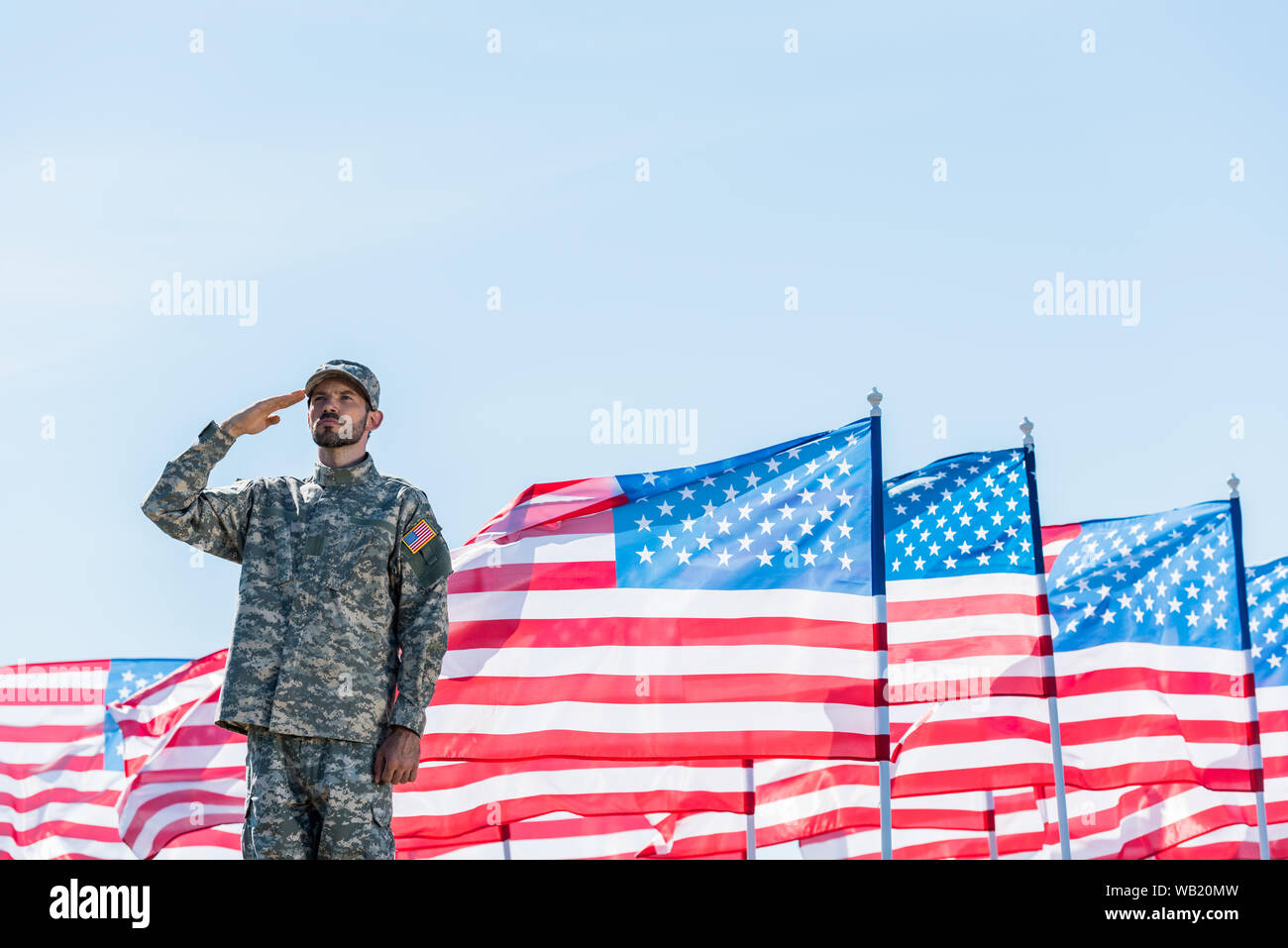 patriotic soldier in military uniform giving salute near american flags ...