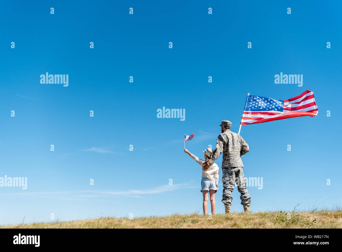 back view of child in straw hat and military father holding american ...