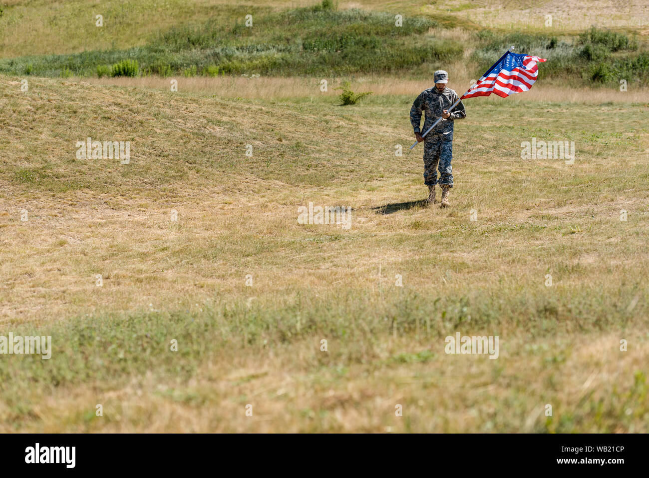 selective focus of handsome soldier in uniform walking and holding ...