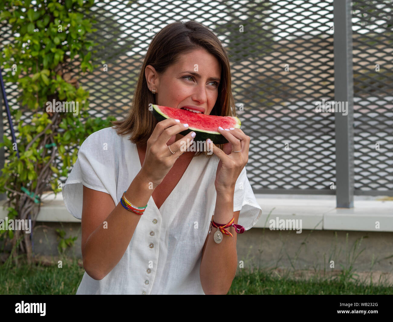 Caucasian woman eating watermelon slices in the garden of her house and ...