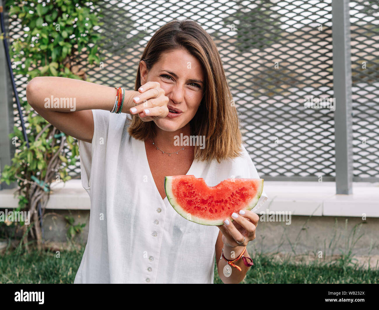 Caucasian woman eating watermelon slices in the garden of her house and ...