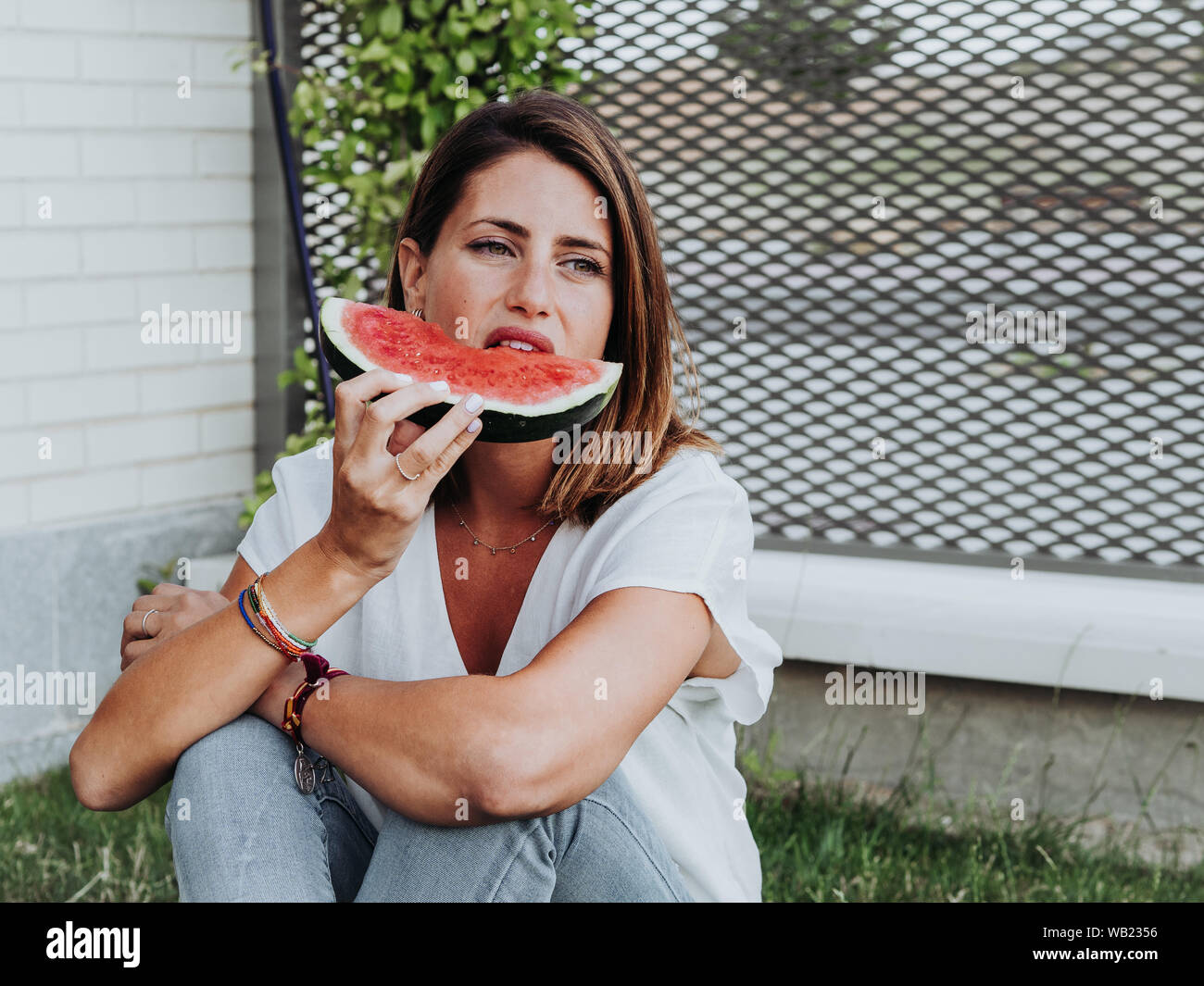 Caucasian woman eating watermelon slices in the garden of her house and ...