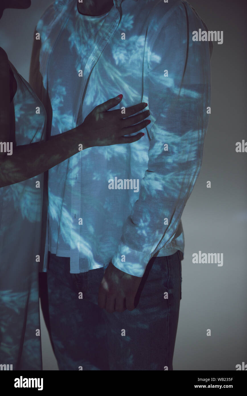cropped view of two people standing in darkness and hugging each other ...
