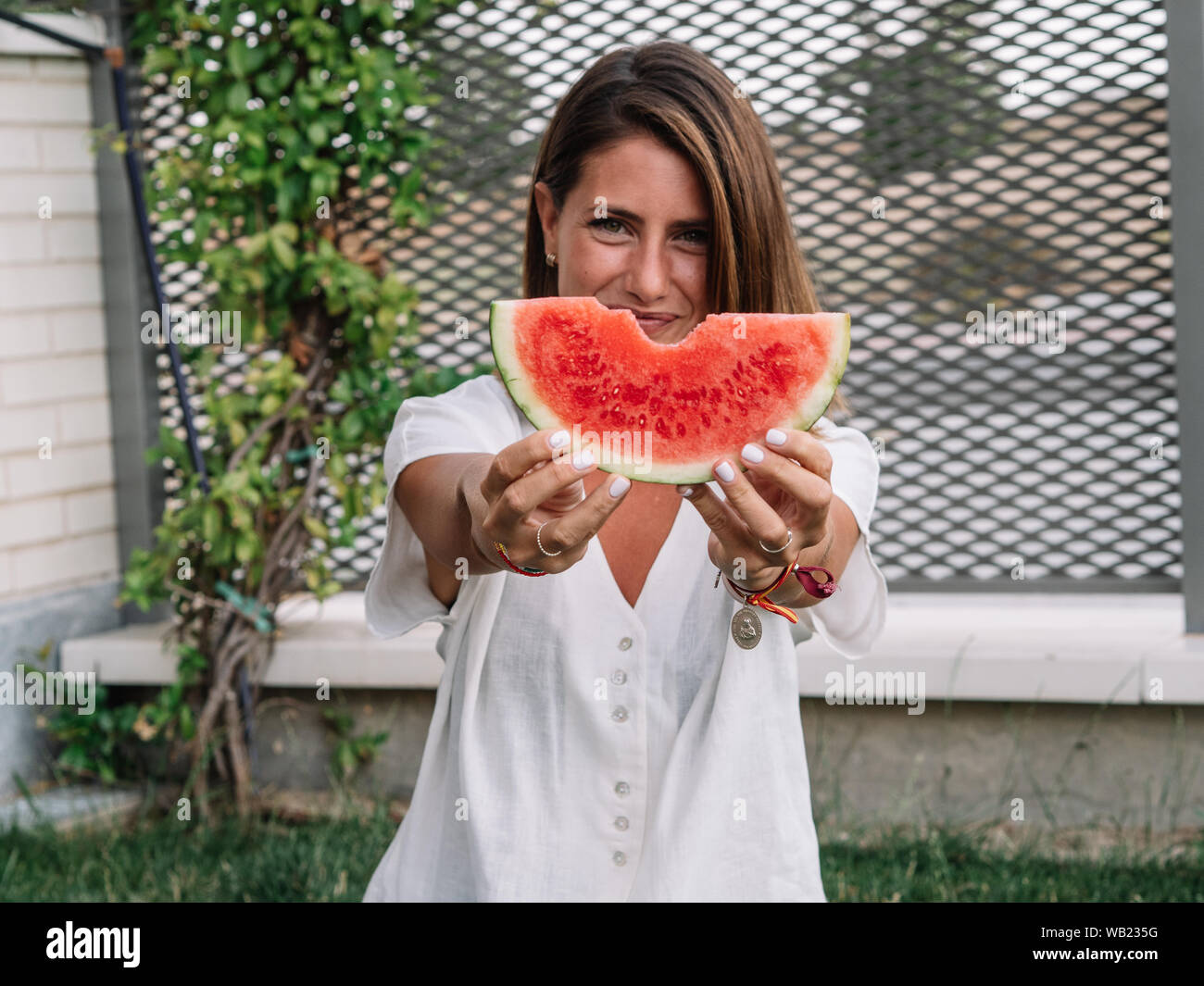 Caucasian woman eating watermelon slices in the garden of her house and ...