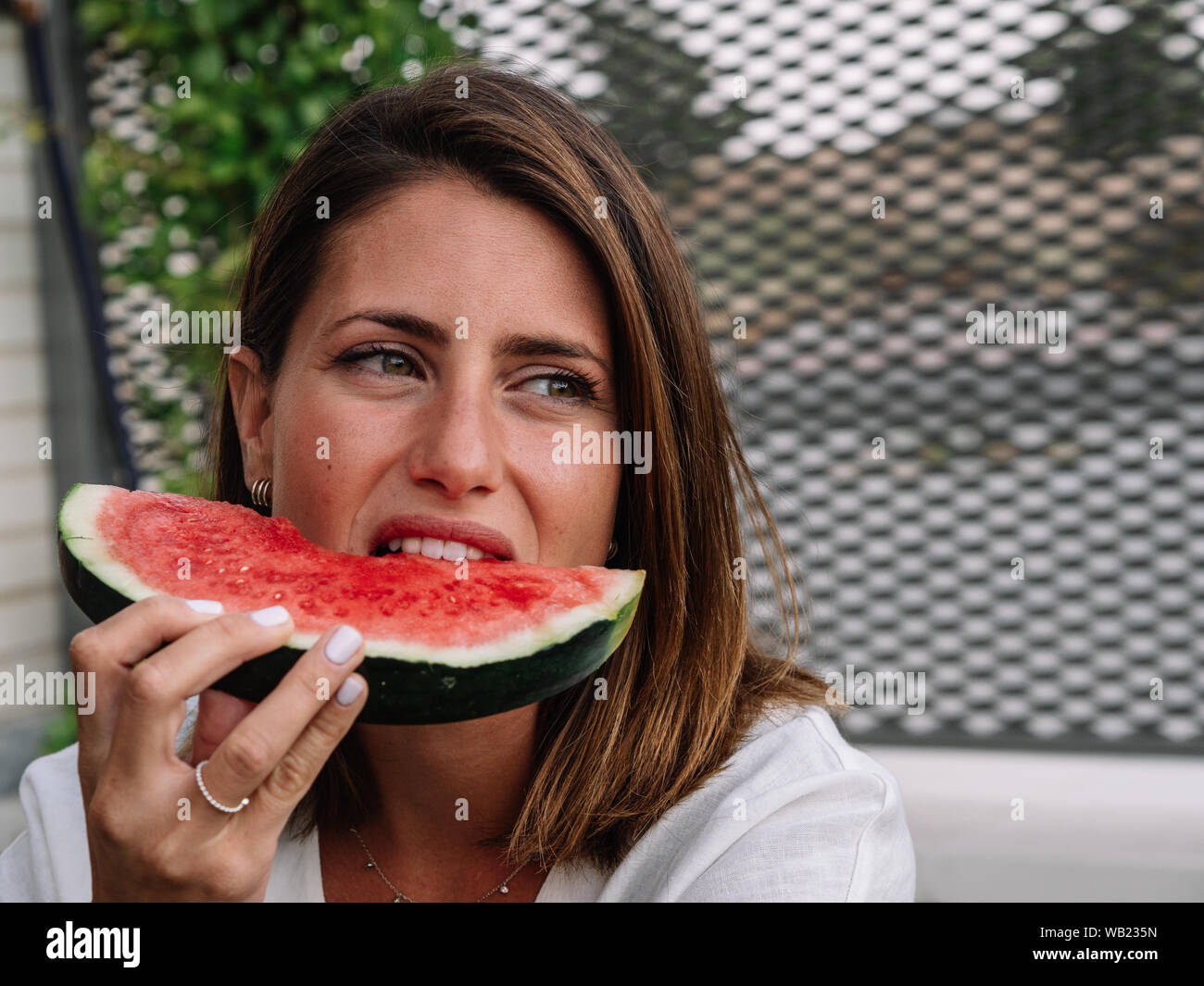 Caucasian woman eating watermelon slices in the garden of her house and ...