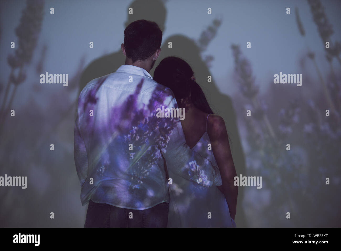 back view of girl and man hugging while standing in darkness on light ...