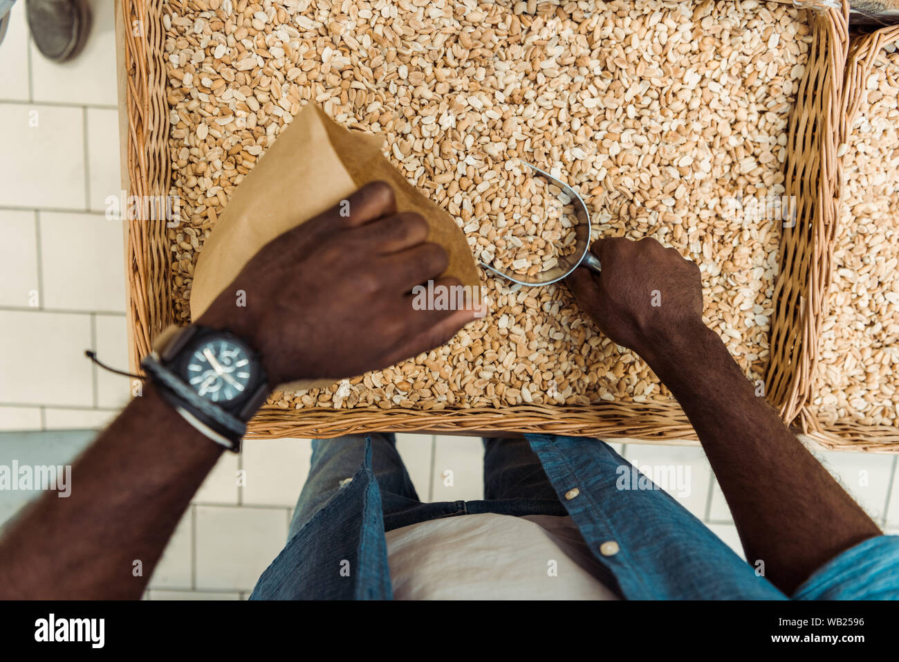 top view of african american man holding metal scoop with tasty peanuts ...