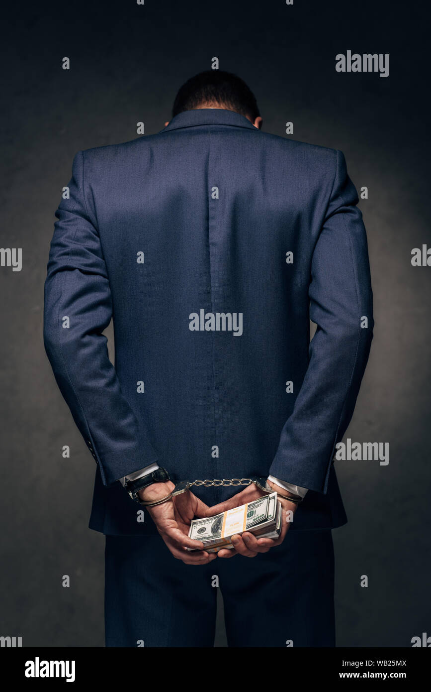 back view of handcuffed man in suit holding bribe on grey Stock Photo ...