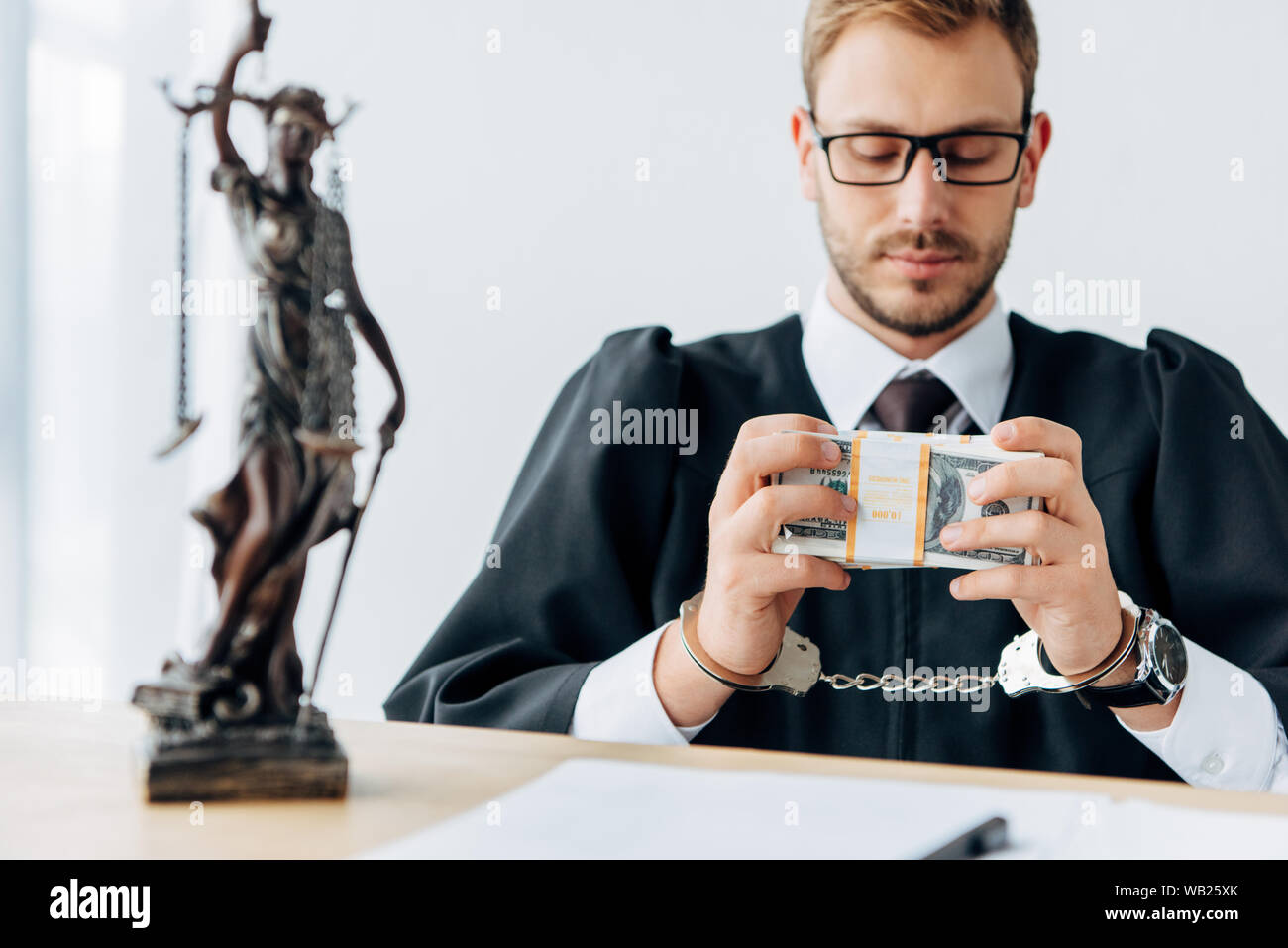 selective focus of statuette of justice near handsome handcuffed judge ...