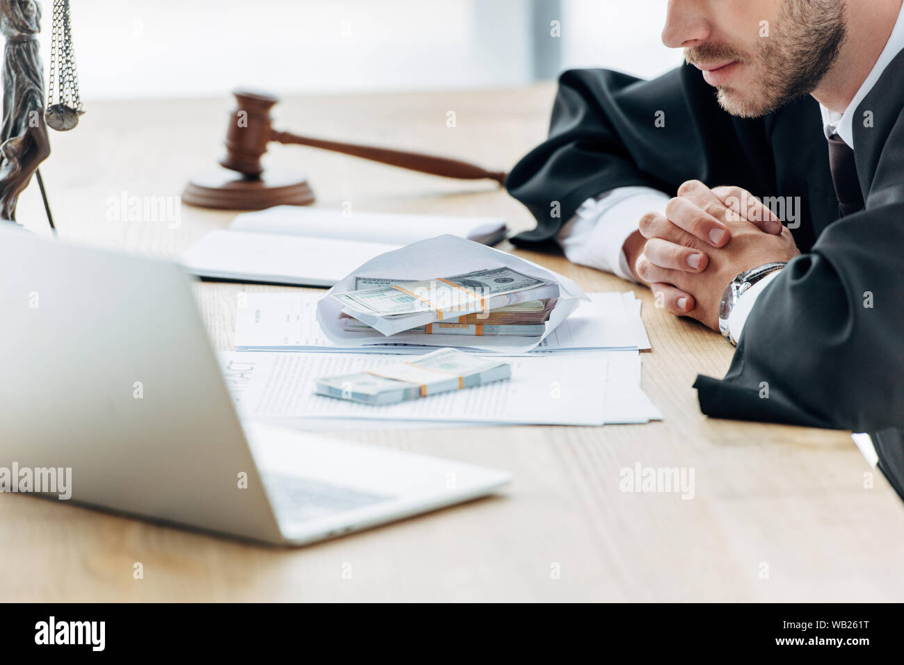 cropped view of man holding money while sitting near wooden judge gavel ...