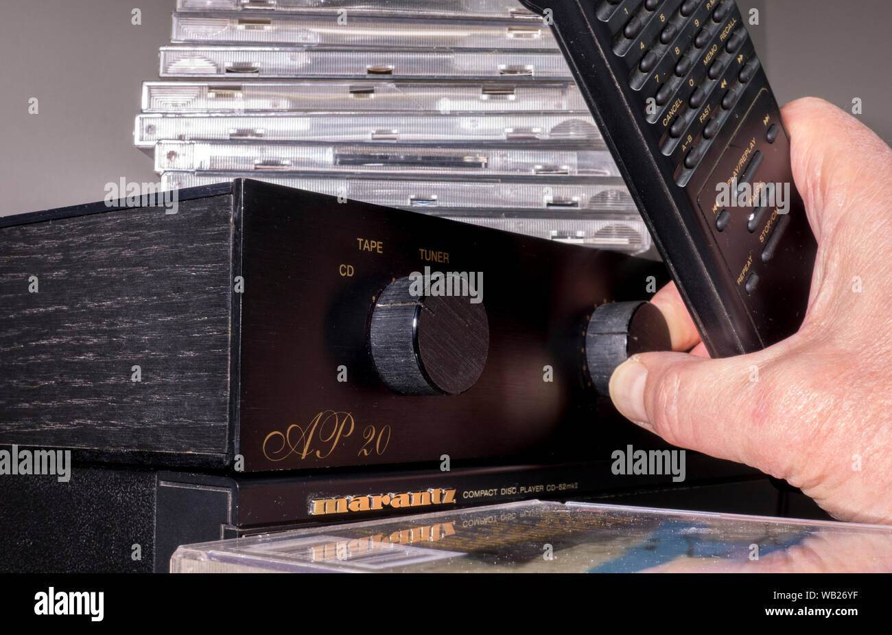 A man’s hand holding a remote control while turning a rotary volume ...