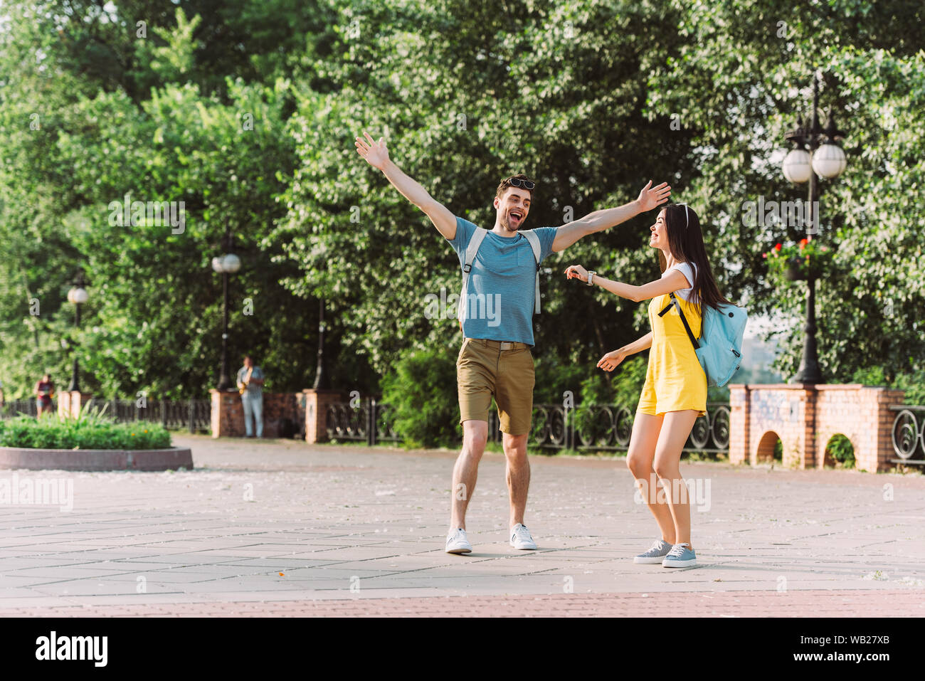 handsome man and asian woman with outstretched hands smiling outside ...