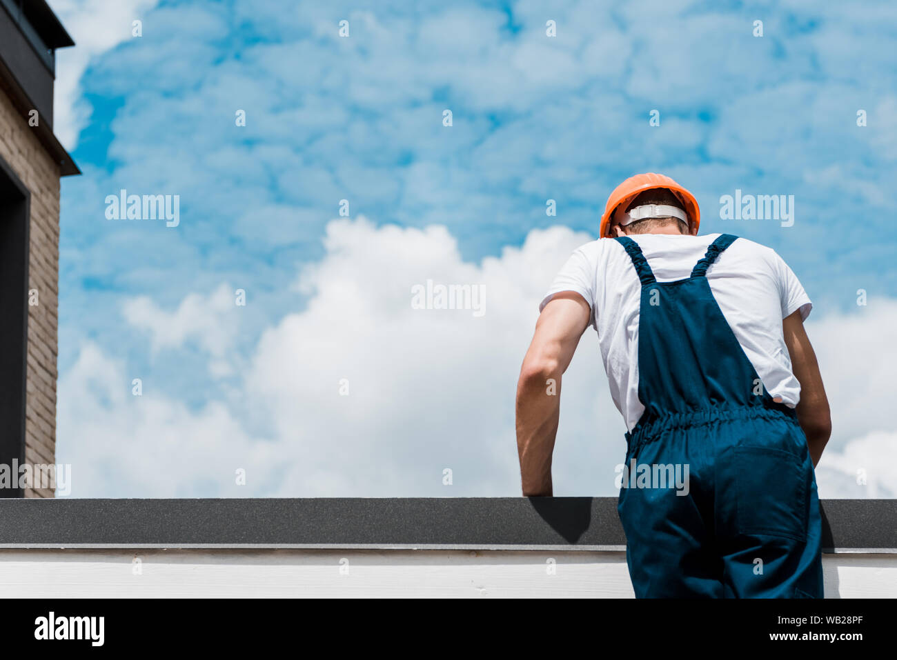back view of repairman in helmet and uniform standing against blue sky ...