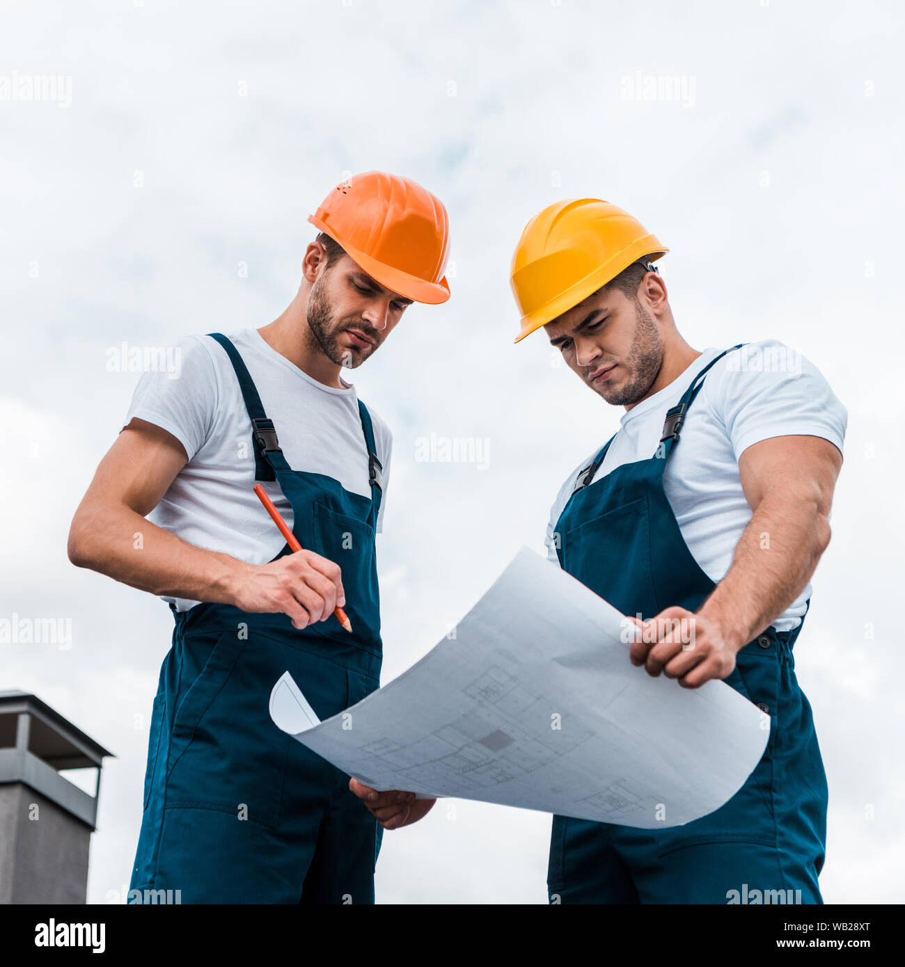 low angle view of handsome builders in uniform looking at paper with ...