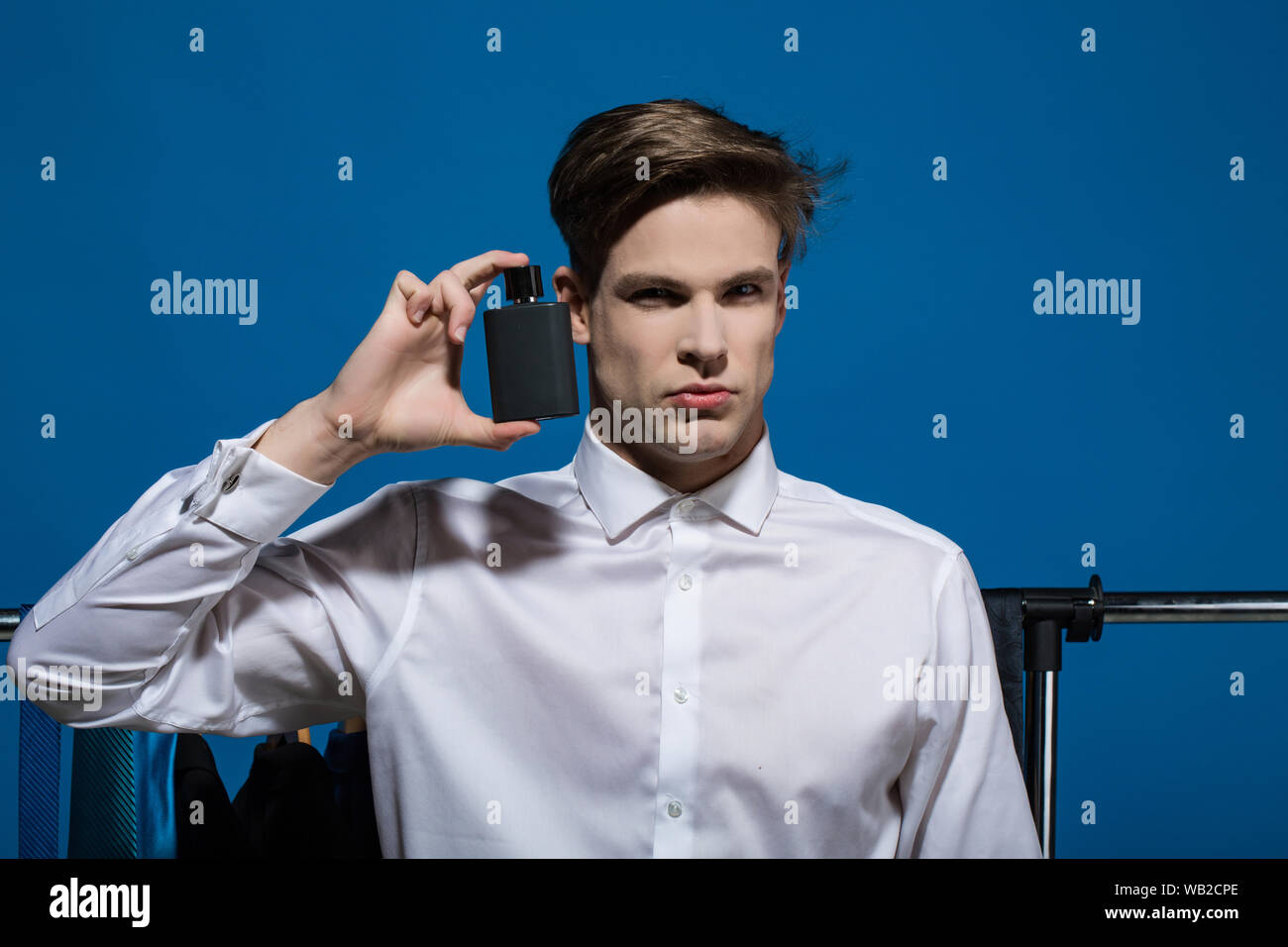 Businessman hold perfume in wardrobe on blue background. Man in white ...