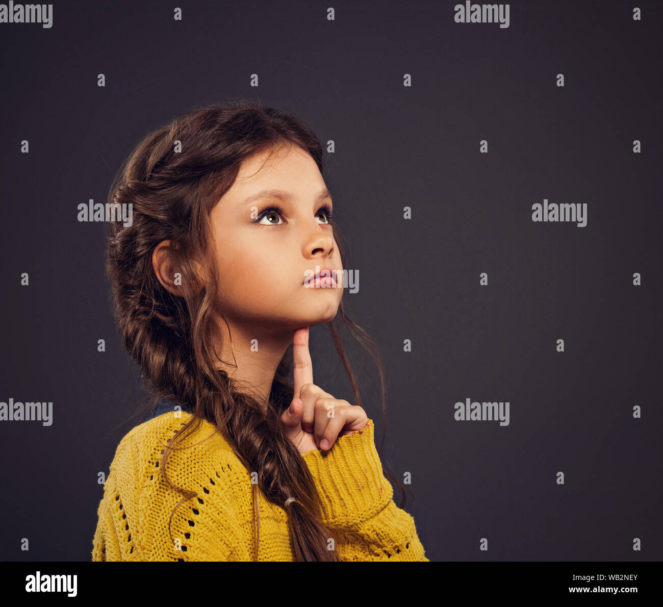 Thinking dreamy serious cute kid girl looking up on grey studio ...