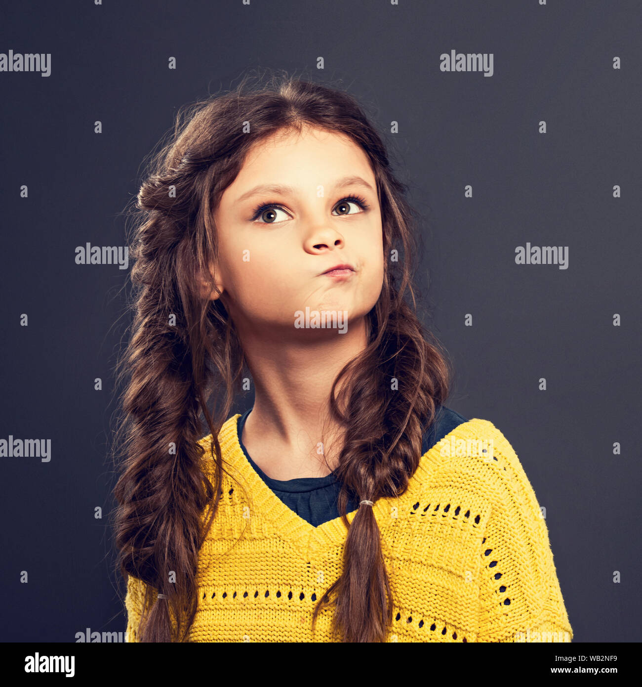 Thinking dreamy grimacing kid girl looking up on grey studio background ...