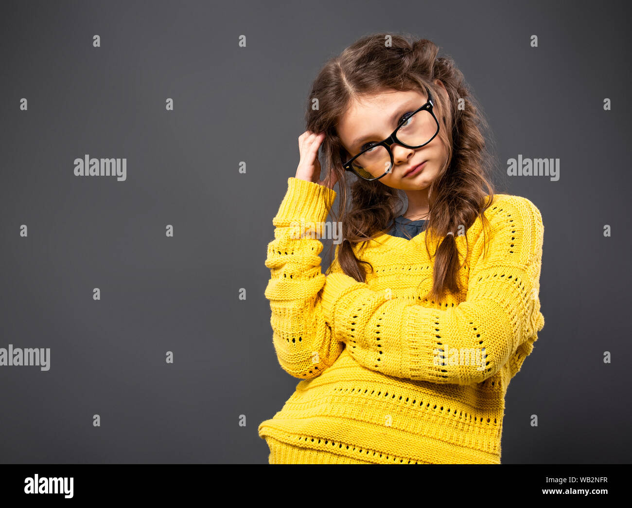 Thinking serious kid girl scratch the head in eyeglasses on grey studio ...
