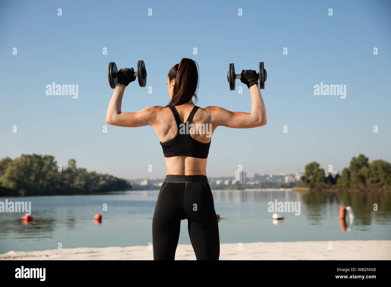 Young healthy woman training upper body with weights at the beach ...