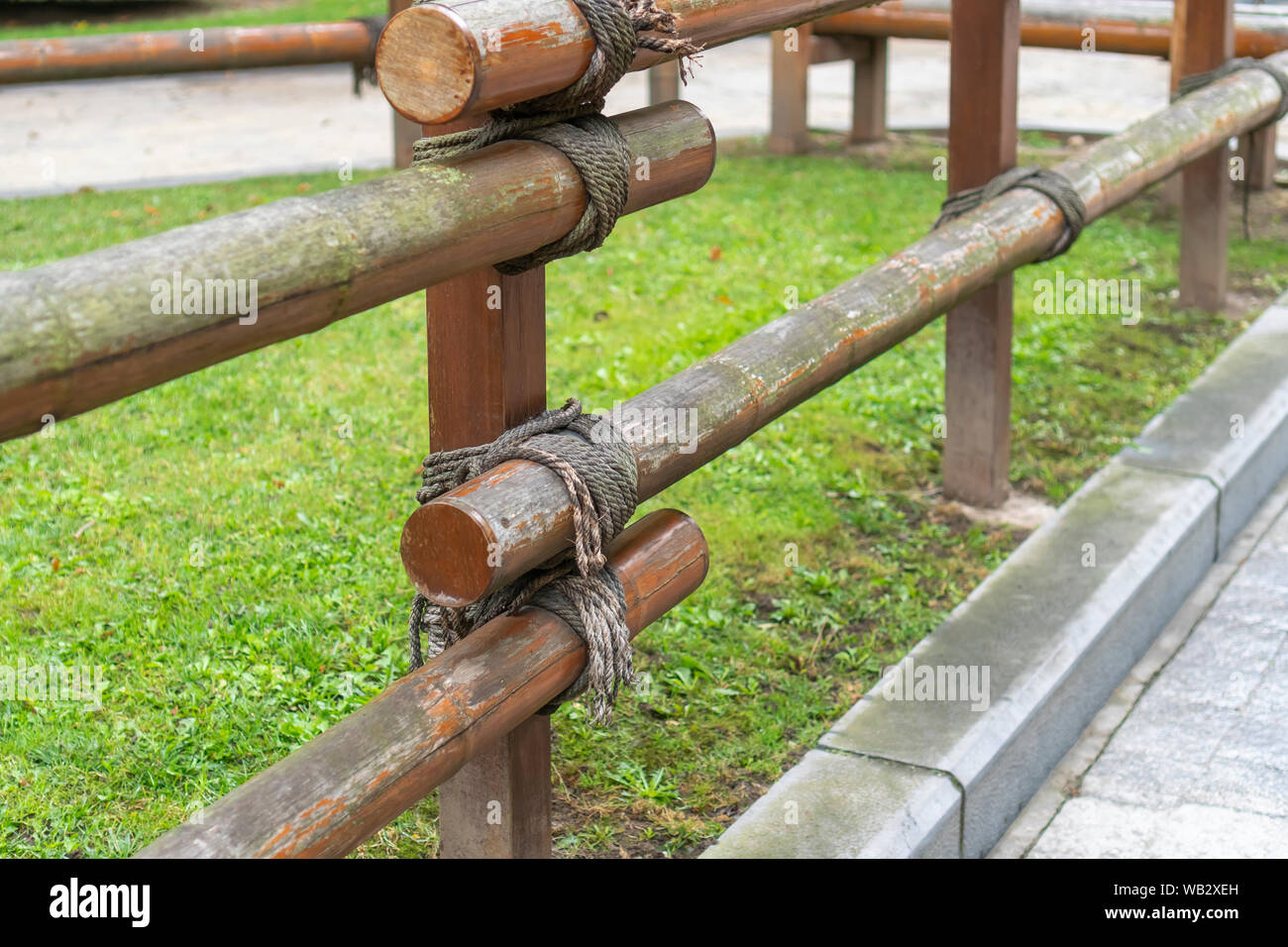 A wooden log fence fixed with a rope in a park next to an asphalt path ...