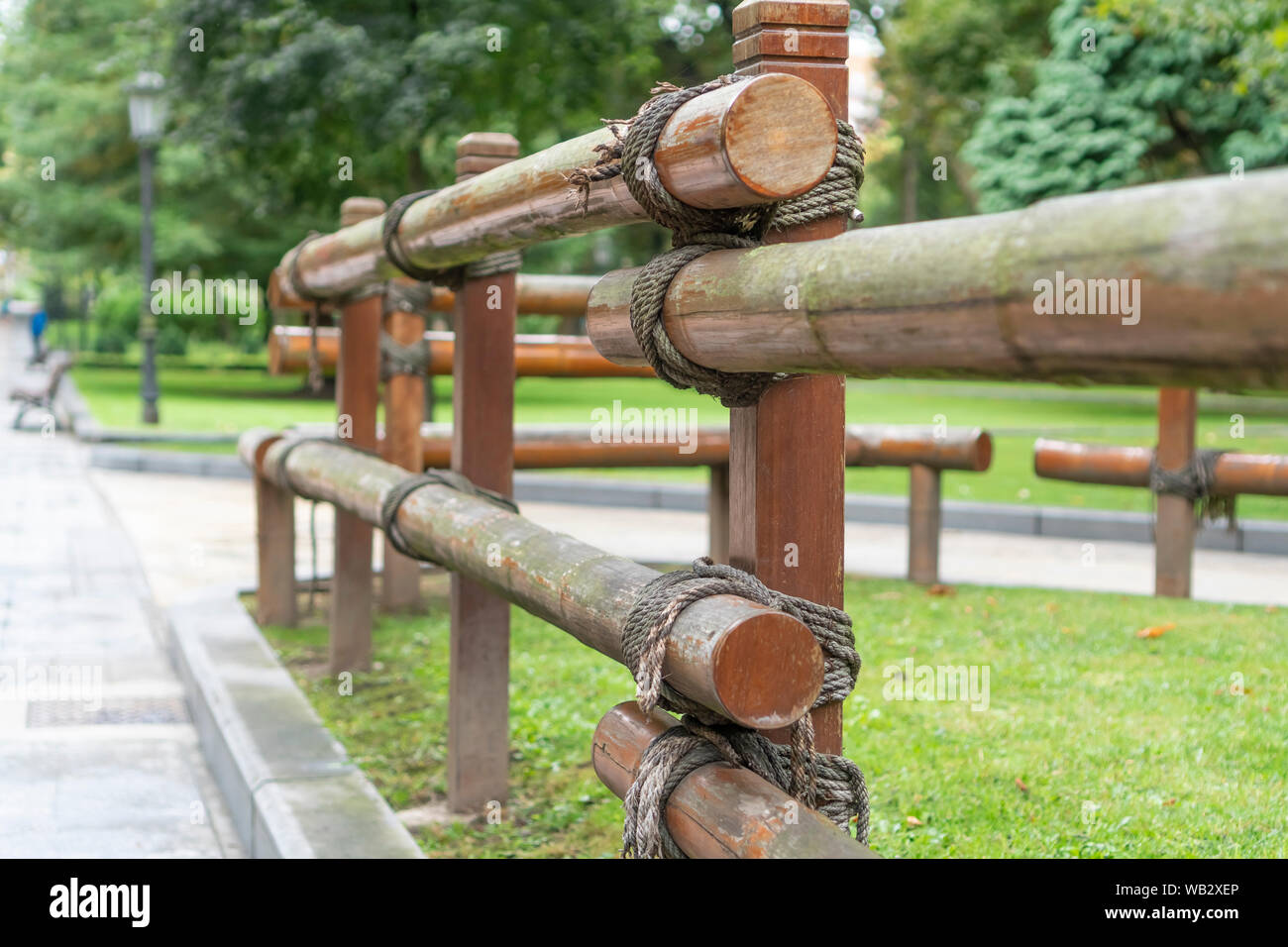 A wooden log fence fixed with a rope in a park next to an asphalt path ...