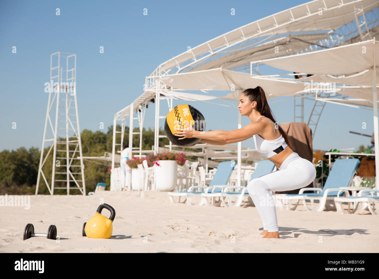 Young healthy woman doing squats with the ball at the beach. Single ...
