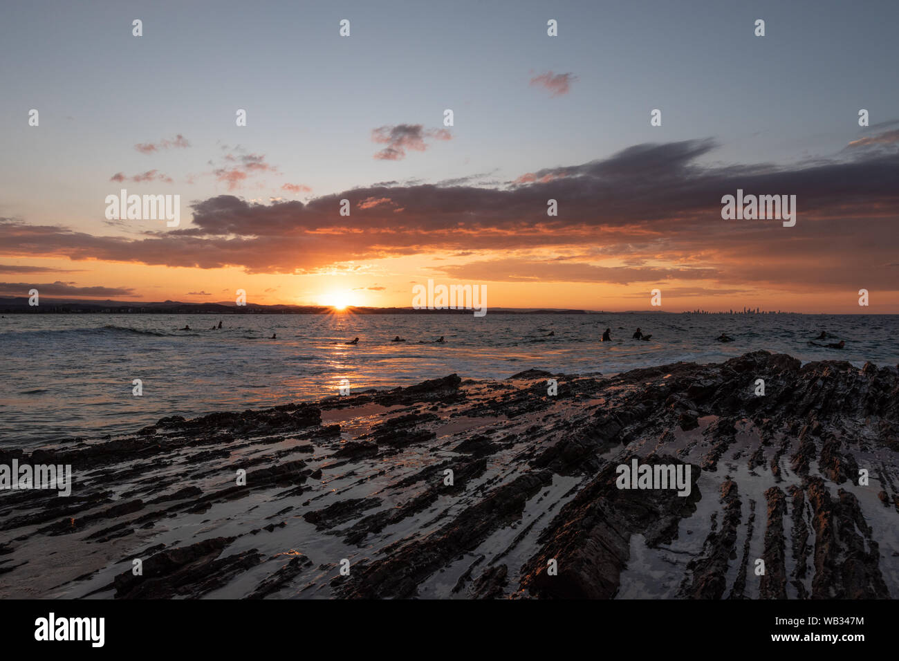 Surfer standing inside water during sunset at Snapper Rocks Stock Photo ...
