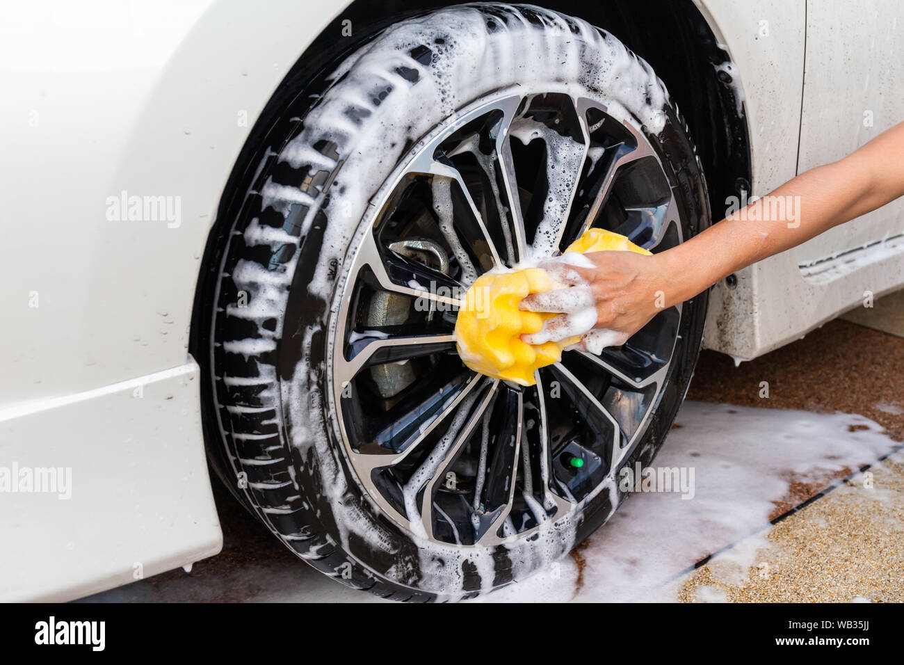 Woman hand with yellow sponge washing wheel modern car or cleaning ...