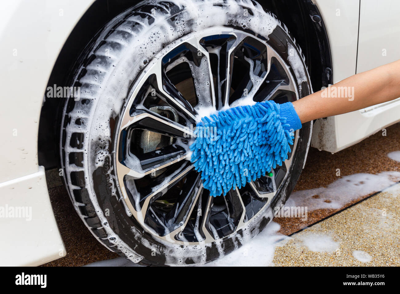 Woman hand with blue microfiber fabric washing wheel modern car or ...