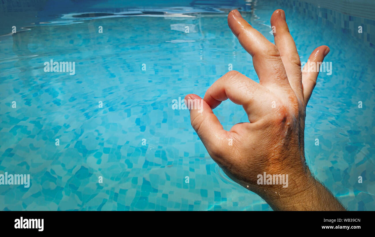 Satisfaction with ok hand gesture over swimming pool blue water ...