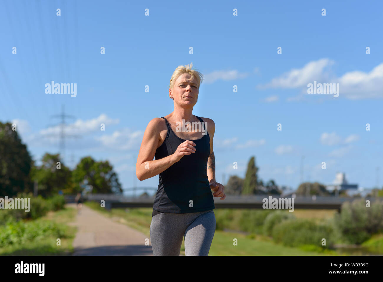 Woman jogging outdoors in summer sunshine approaching the camera in a ...
