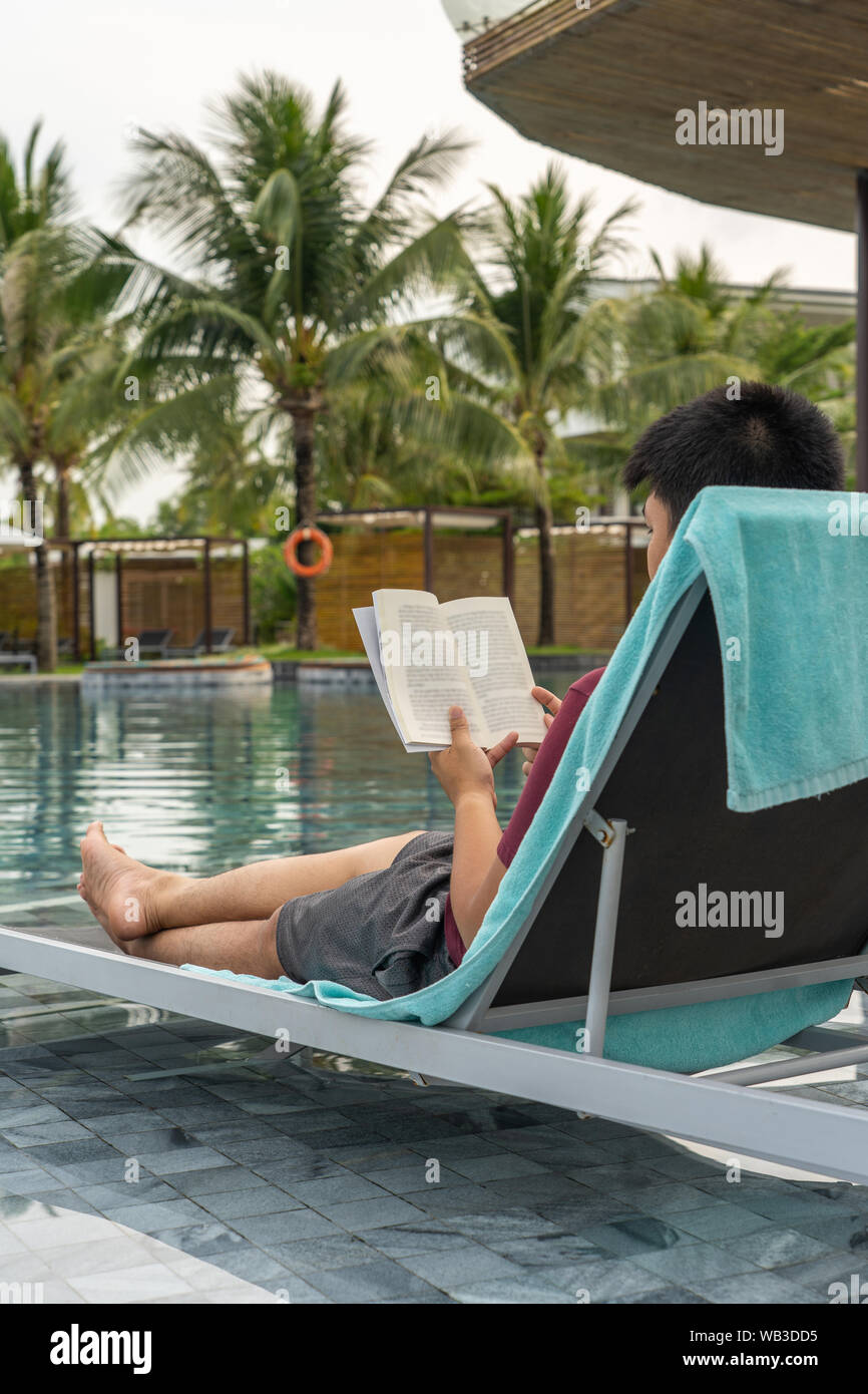 Young Asian man reading book and relaxing at swimming pool Stock Photo ...