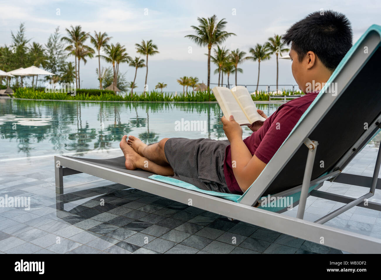Reading book at beautiful swimming pool by the beach Stock Photo - Alamy