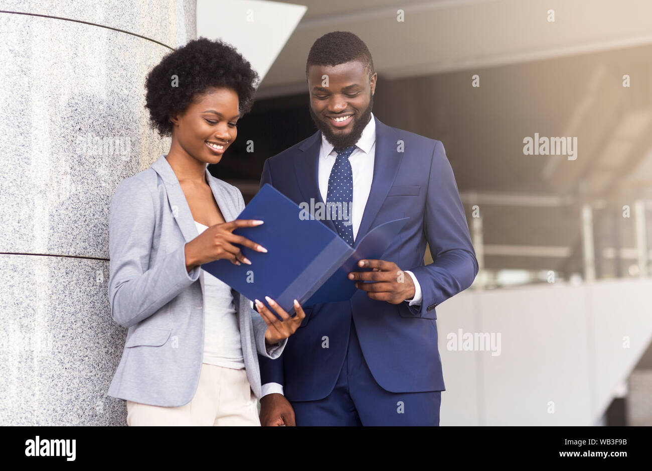 Cheerful businessman and businesswoman working while standing outdoors ...