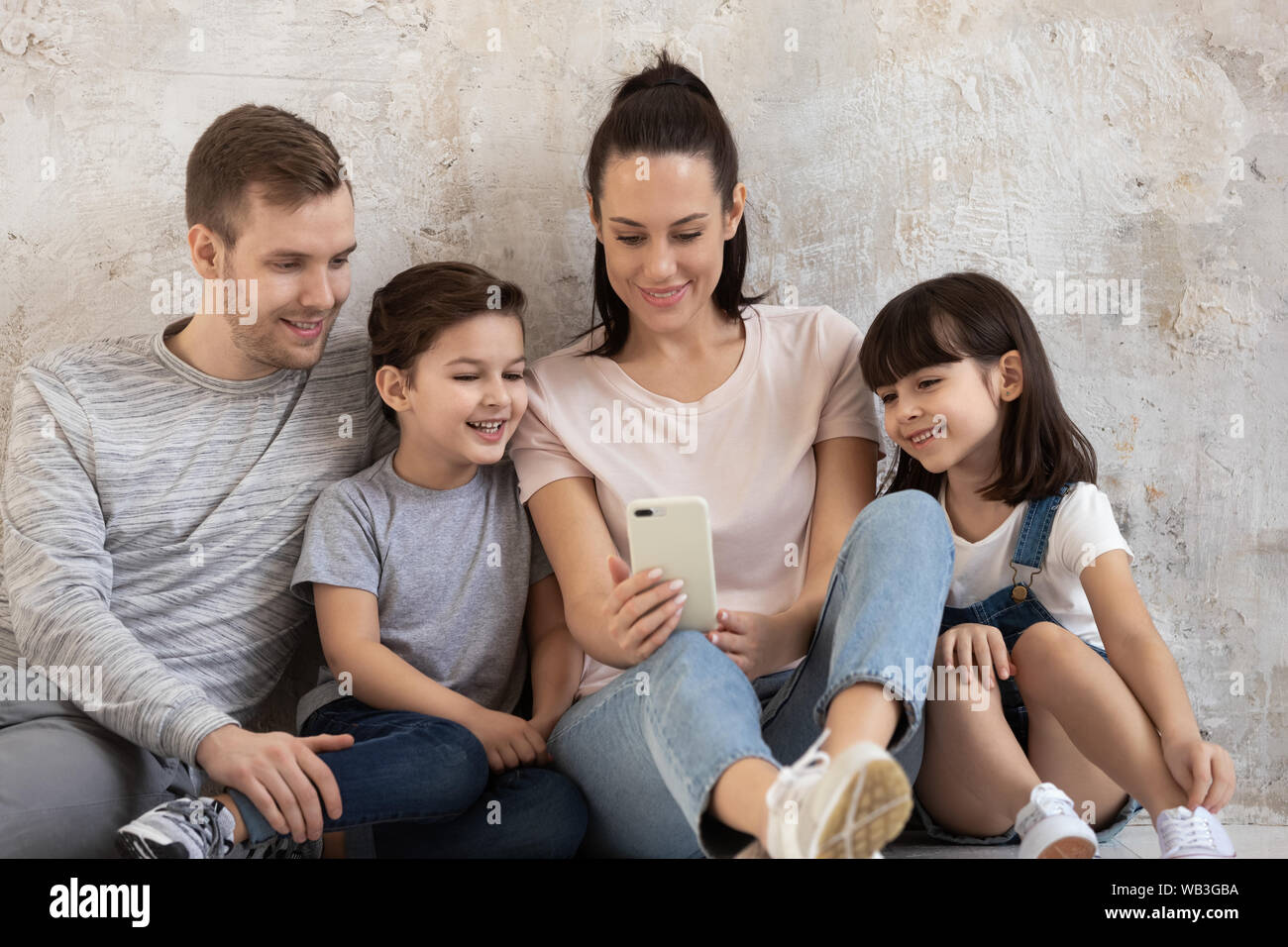 Happy parents with children sit on floor looking at phone Stock Photo ...